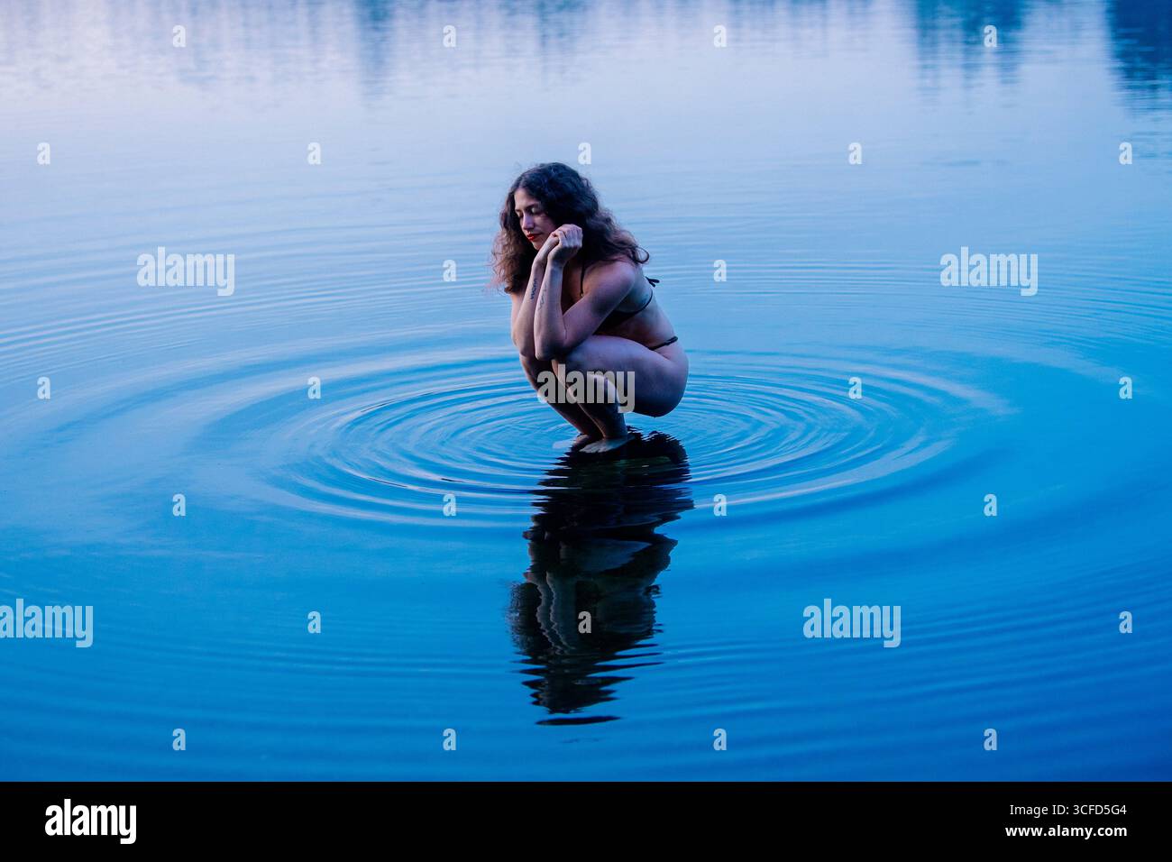 Woman crouching in clear blue water creating ripples around her ...