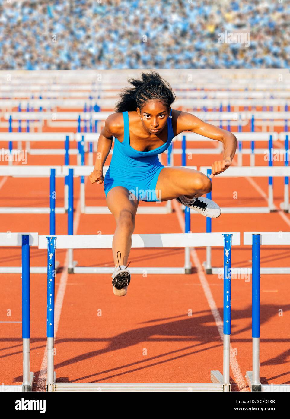 Athlete in blue uniform jumping a hurdle on an outdoor track during a ...