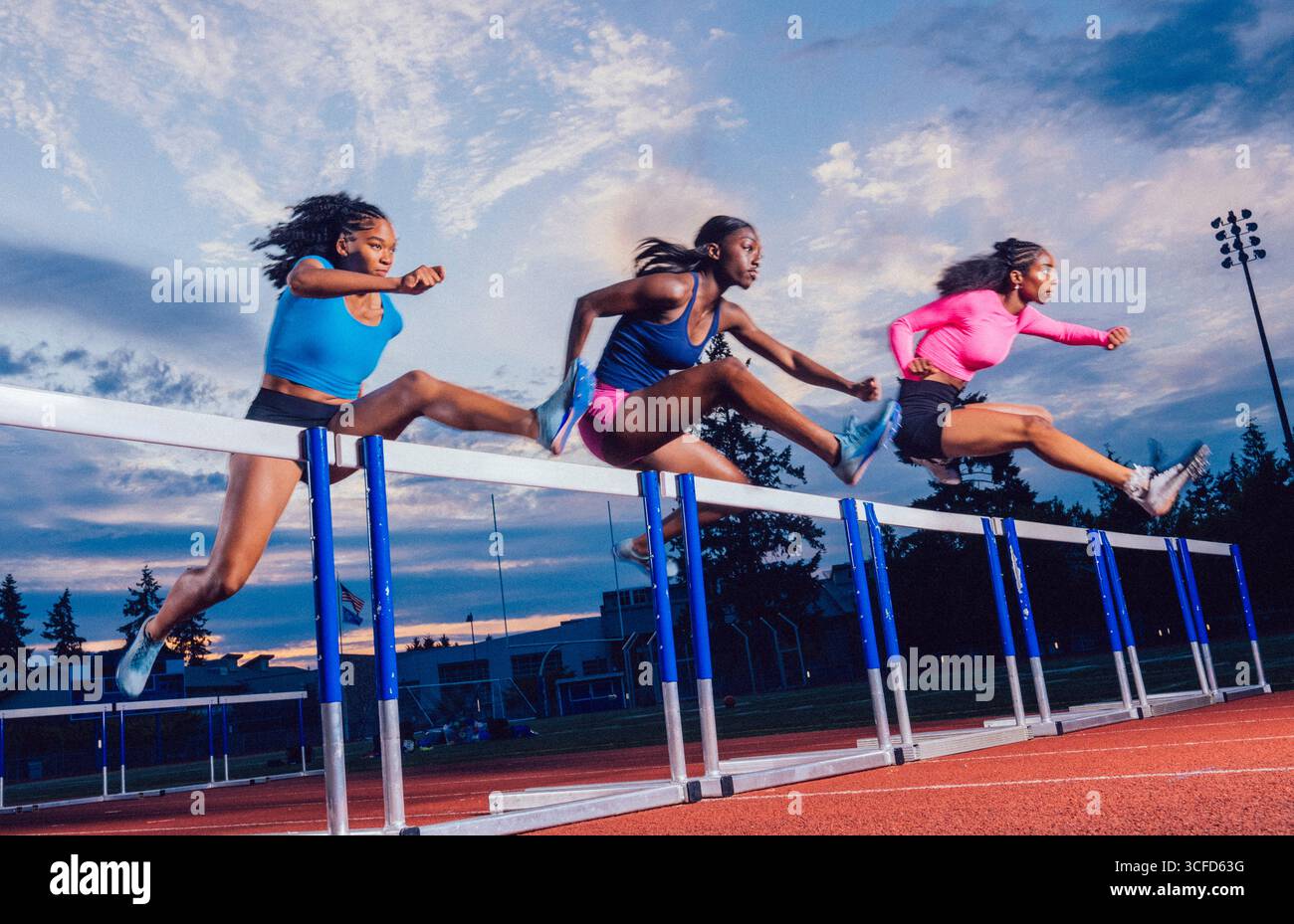 Three athletes in vibrant sportswear jumping hurdles on a track with a ...