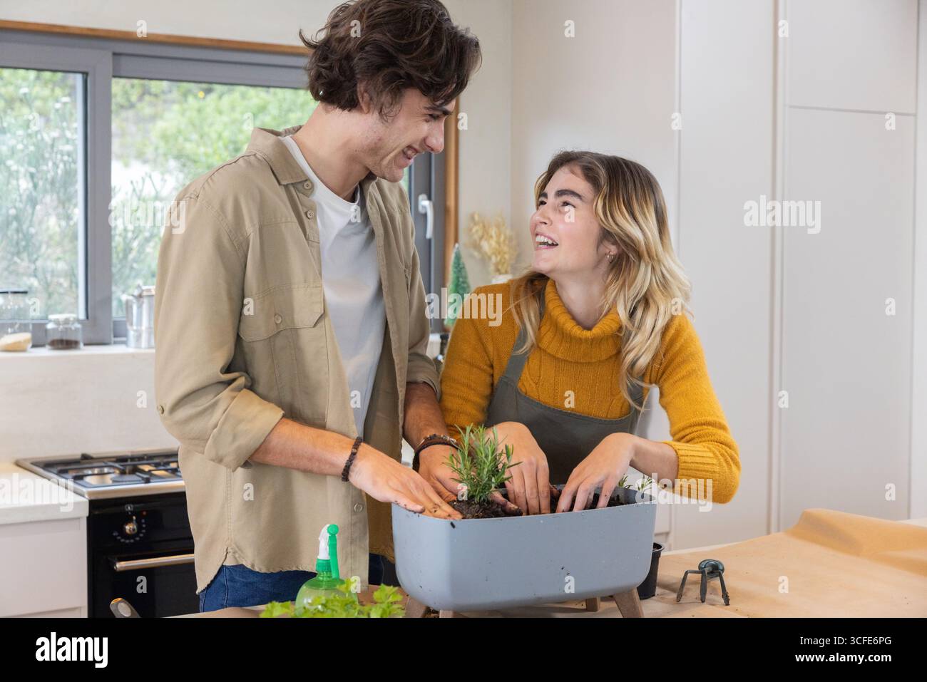 Couple smiling pressing soil around rosemary plant in rectangular ...