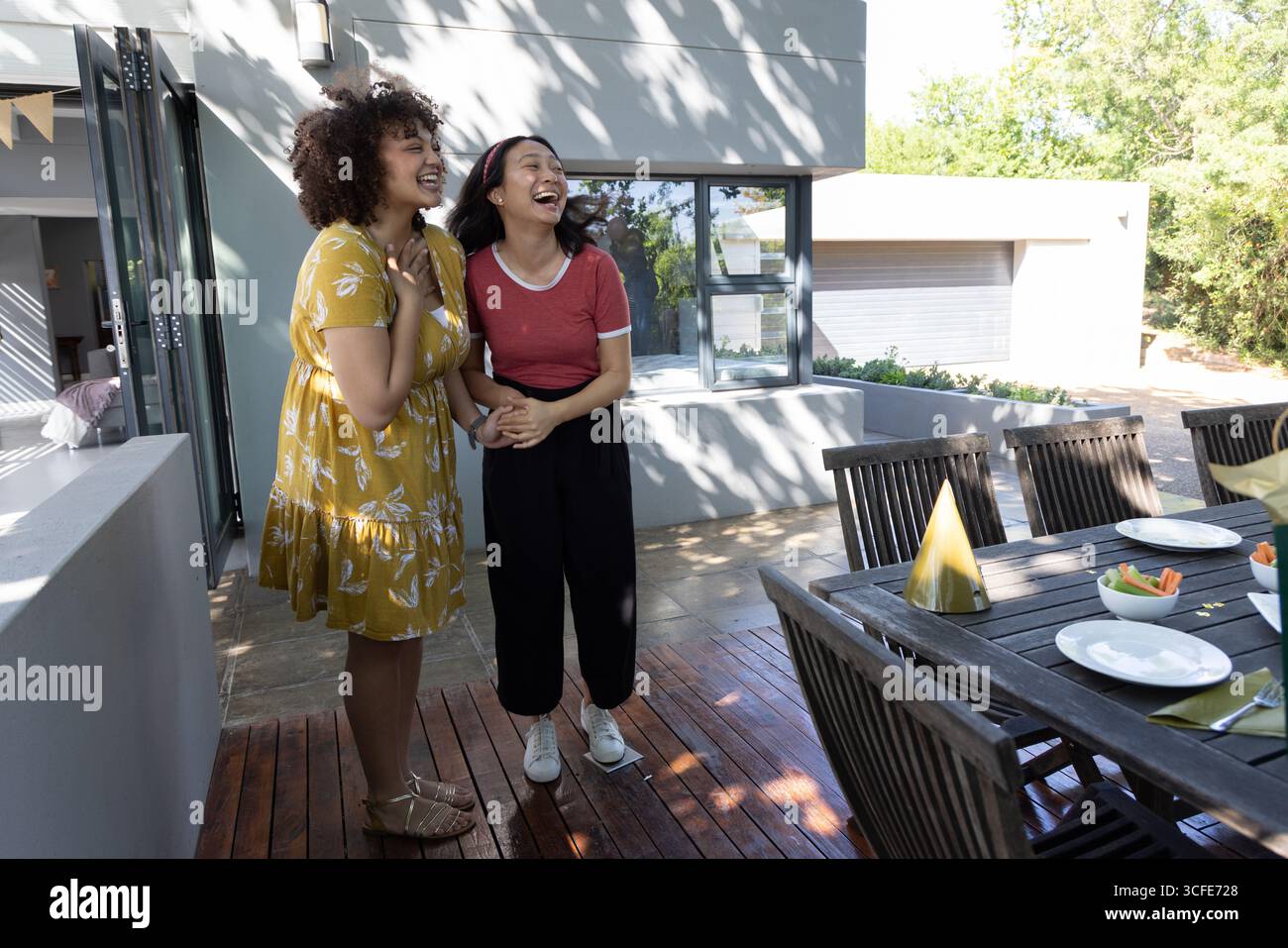 African american and asian female friends laughing and holding hands on ...