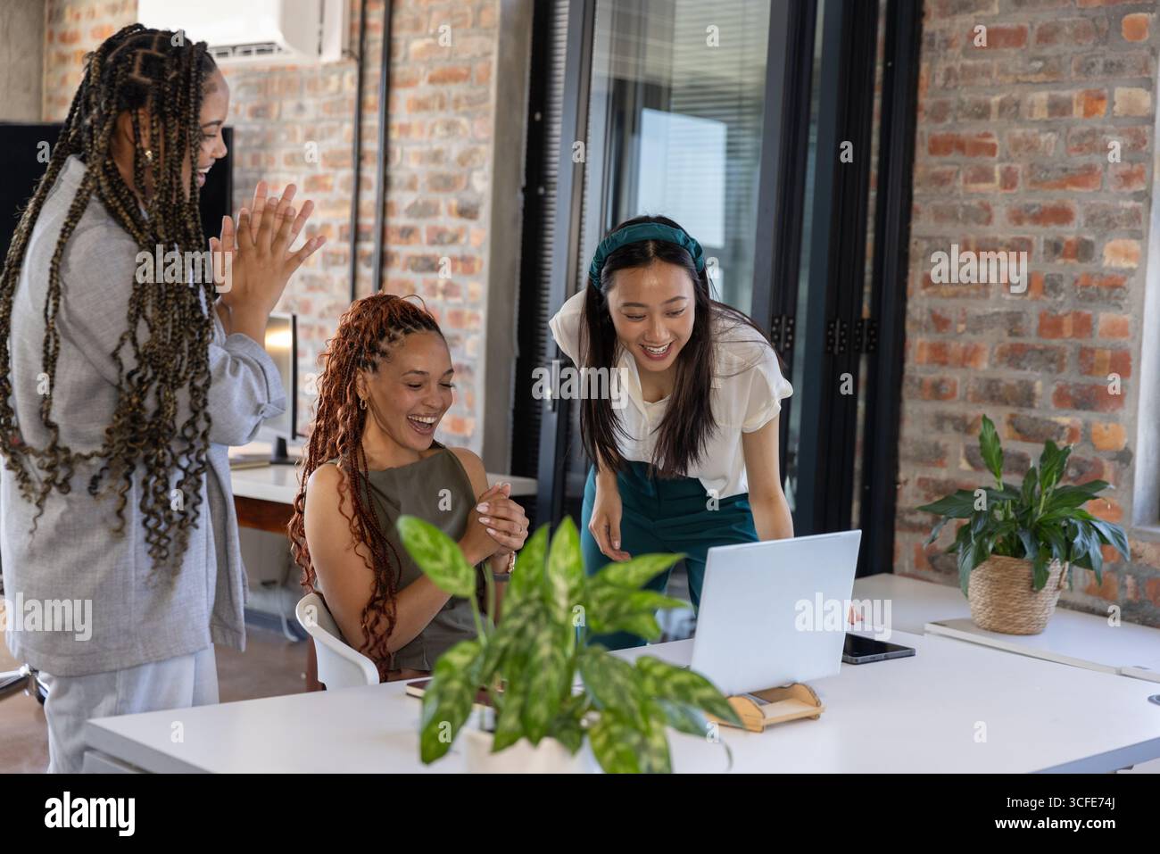 Diverse female coworkers clapping and laughing around laptop and ...