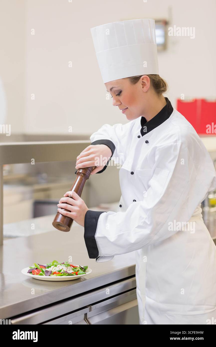 Female chef seasoning green salad with wooden pepper mill on steel ...