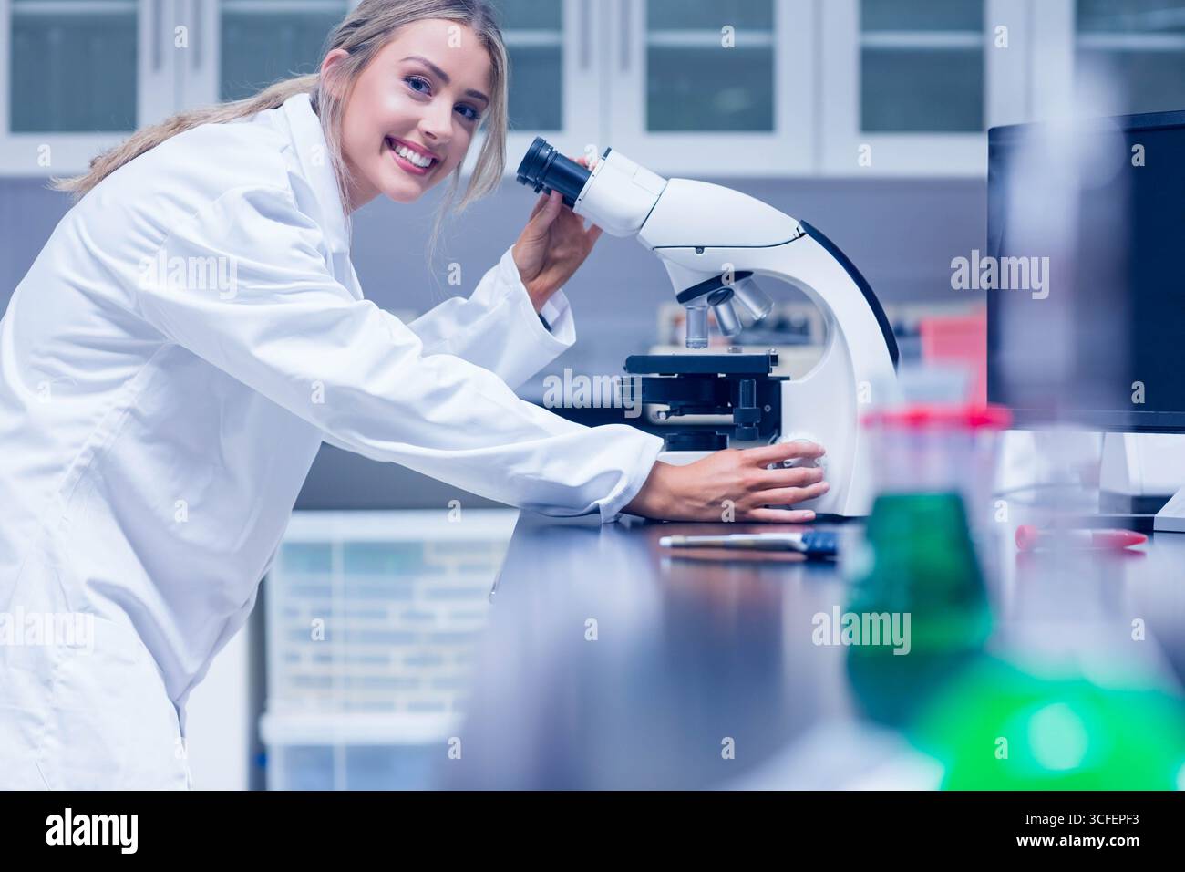 Female scientist leaning over lab bench adjusting microscope stage ...