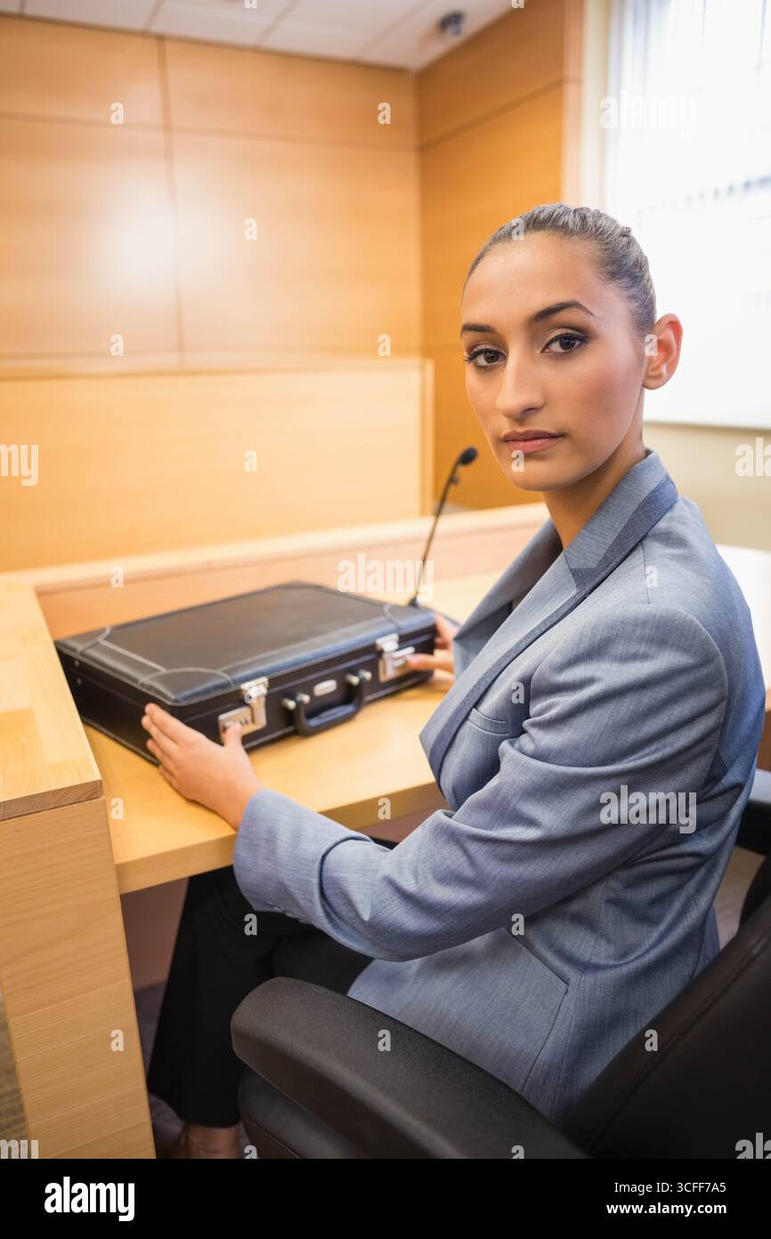 Female lawyer in suit placing briefcase on courtroom witness desk next ...