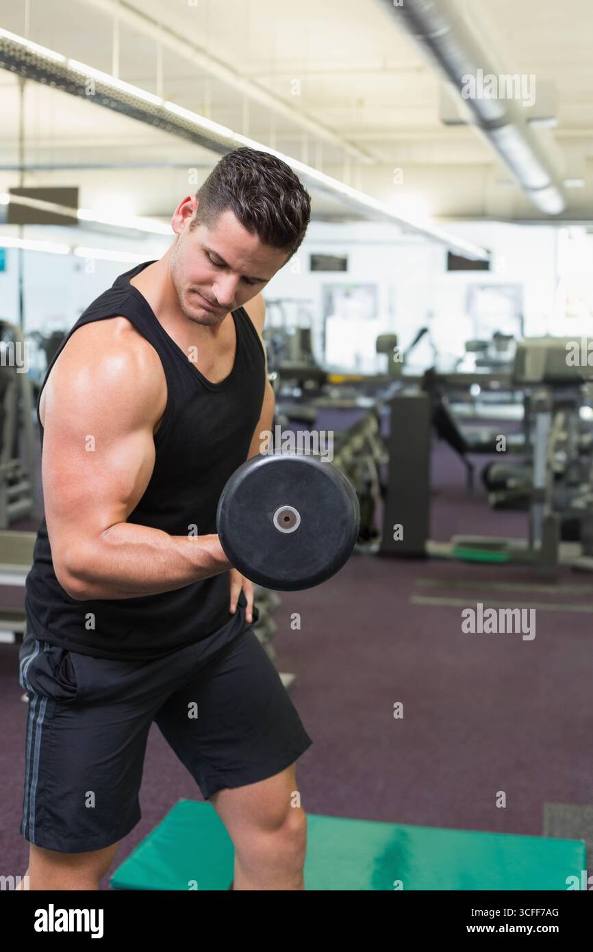 Man lifting heavy dumbbell on green exercise mat in gym weight area ...