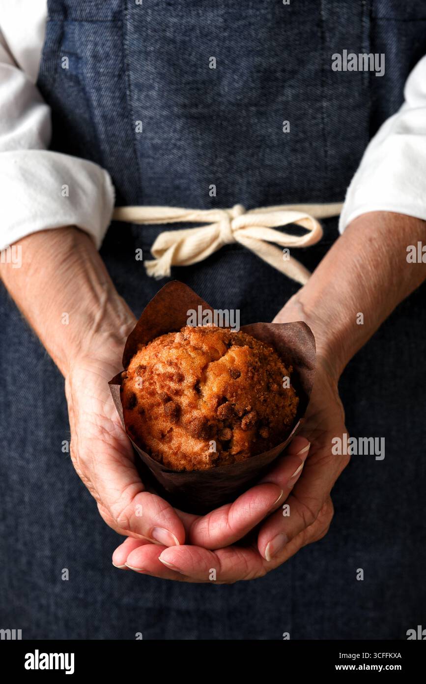A baker holding a fresh baked muffin in her hands. The woman is wearing ...