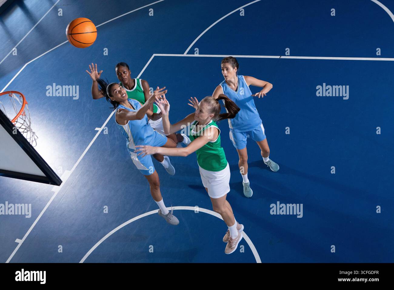 Diverse female opponents jumping and reaching for orange basketball ...