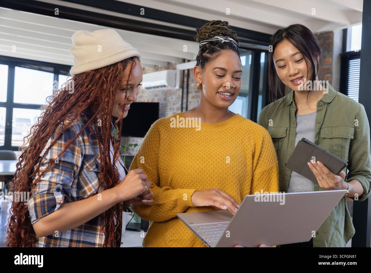 Diverse female coworkers collaborating around laptop at open-plan ...