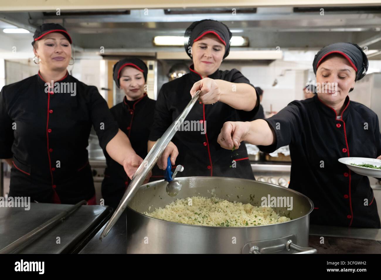 Group of chefs in black uniforms preparing rice in a large pot in a ...