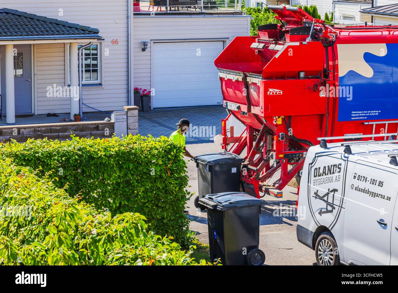Garbage truck worker collecting black trash bins near modern villa on ...