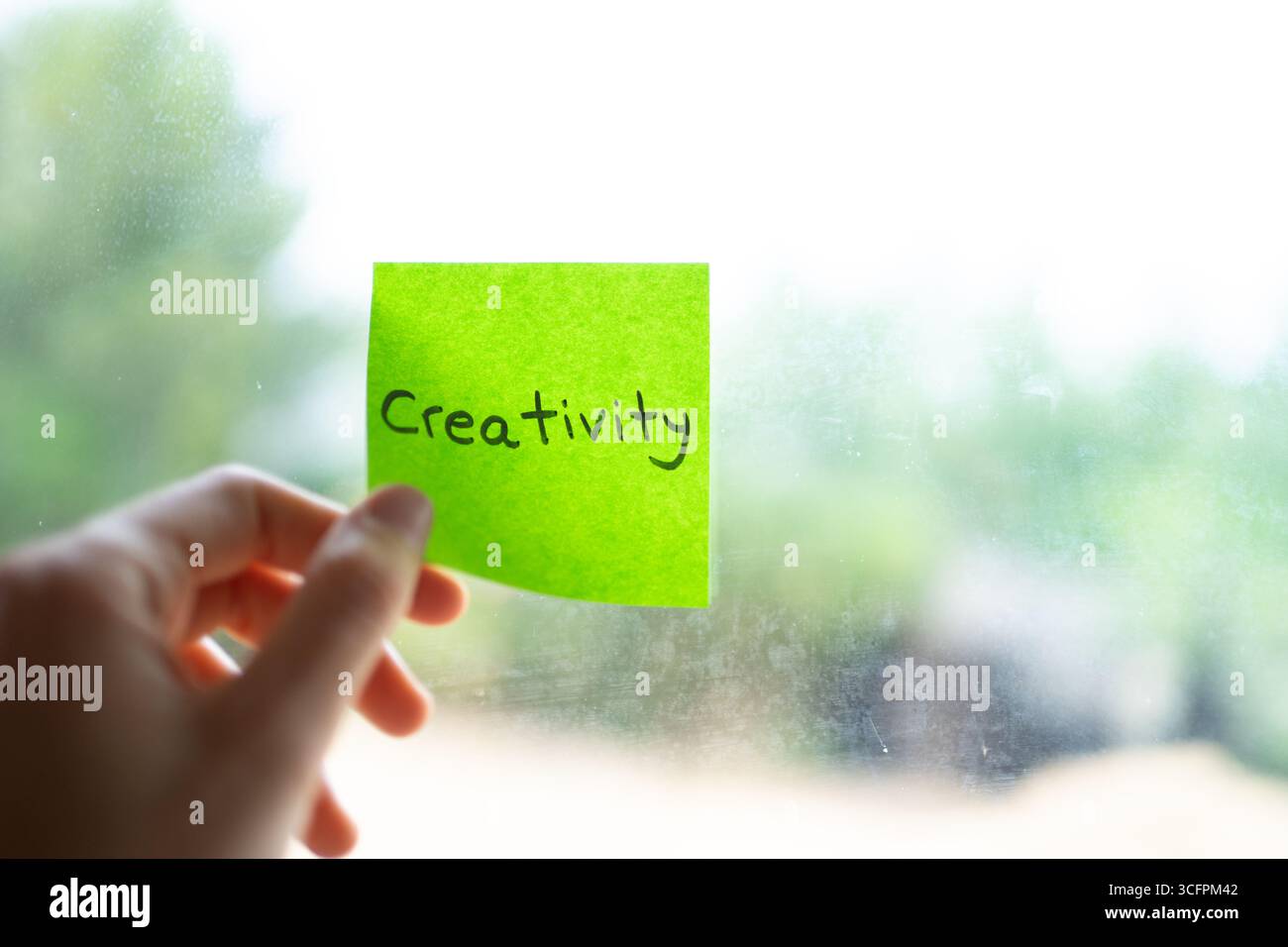 Hand sticking a green adhesive note with the word creativity ...