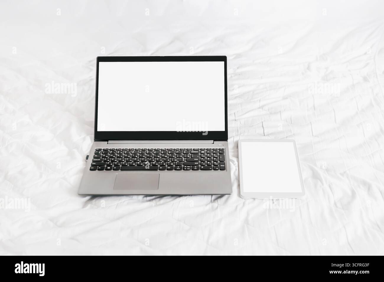 open laptop, tablet with white blank screen on a white bed. grey laptop ...