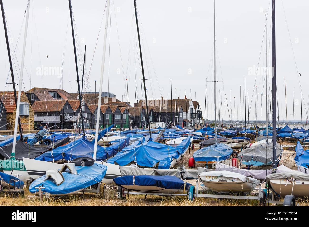 Whitstable Harbour dinghies on shingle beach, masts and boatyard sheds ...