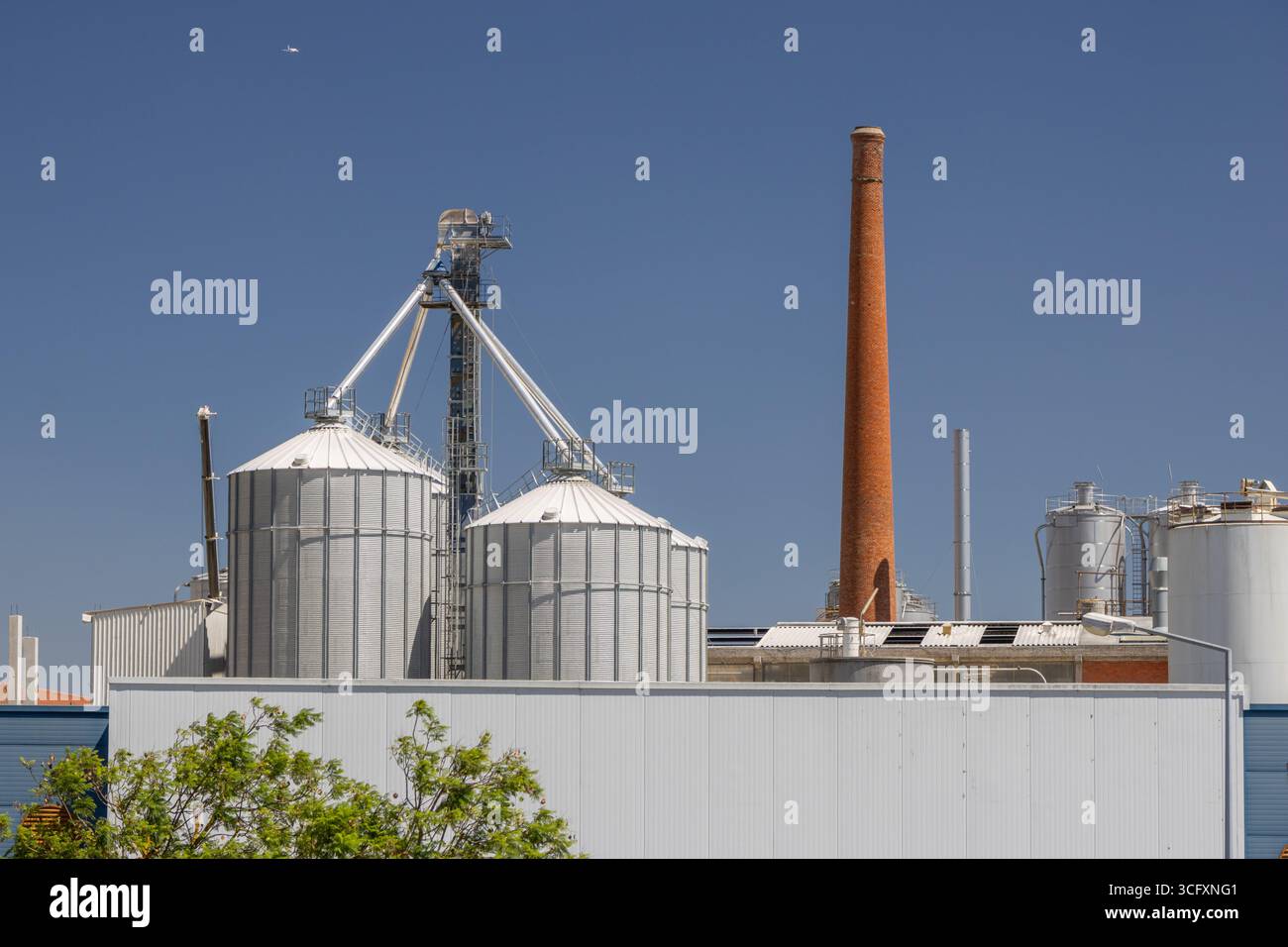 Metal silos and a tall brick chimney dominate the skyline of a modern ...