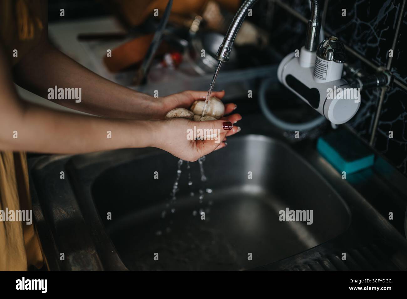 Washing fresh produce under running tap water in a modern kitchen sink ...