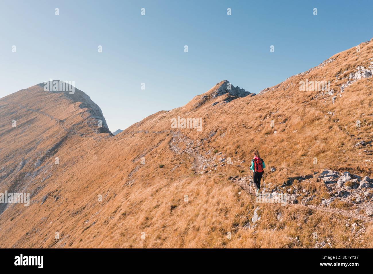 Female hikes on a rugged path surrounded by golden grass and rocky ...