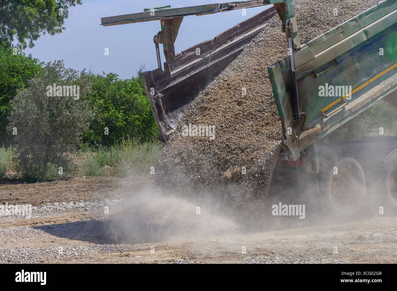A dump truck unloads gravel for a new road project, forming the ...