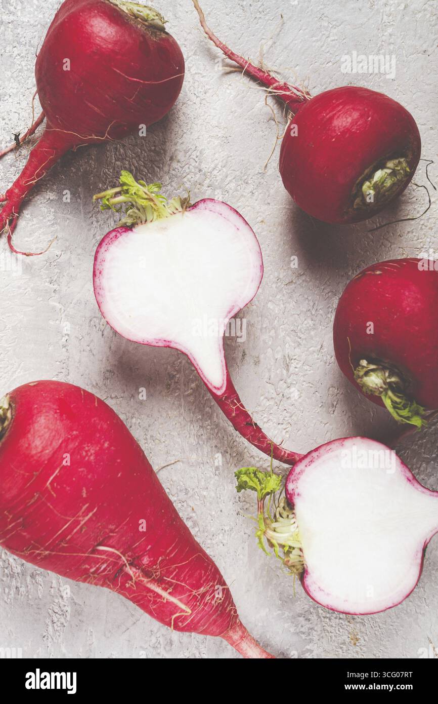 Bright red radishes are arranged on a counter, with one radish cut in ...