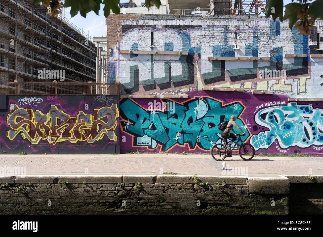 A cyclist rides past graffiti art along Regent's Canal in Hackney Wick ...