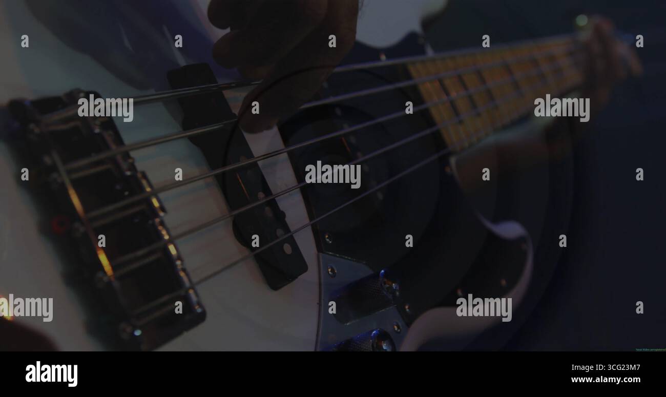 Plucking musician's hand exploring white electric bass strings on dim ...