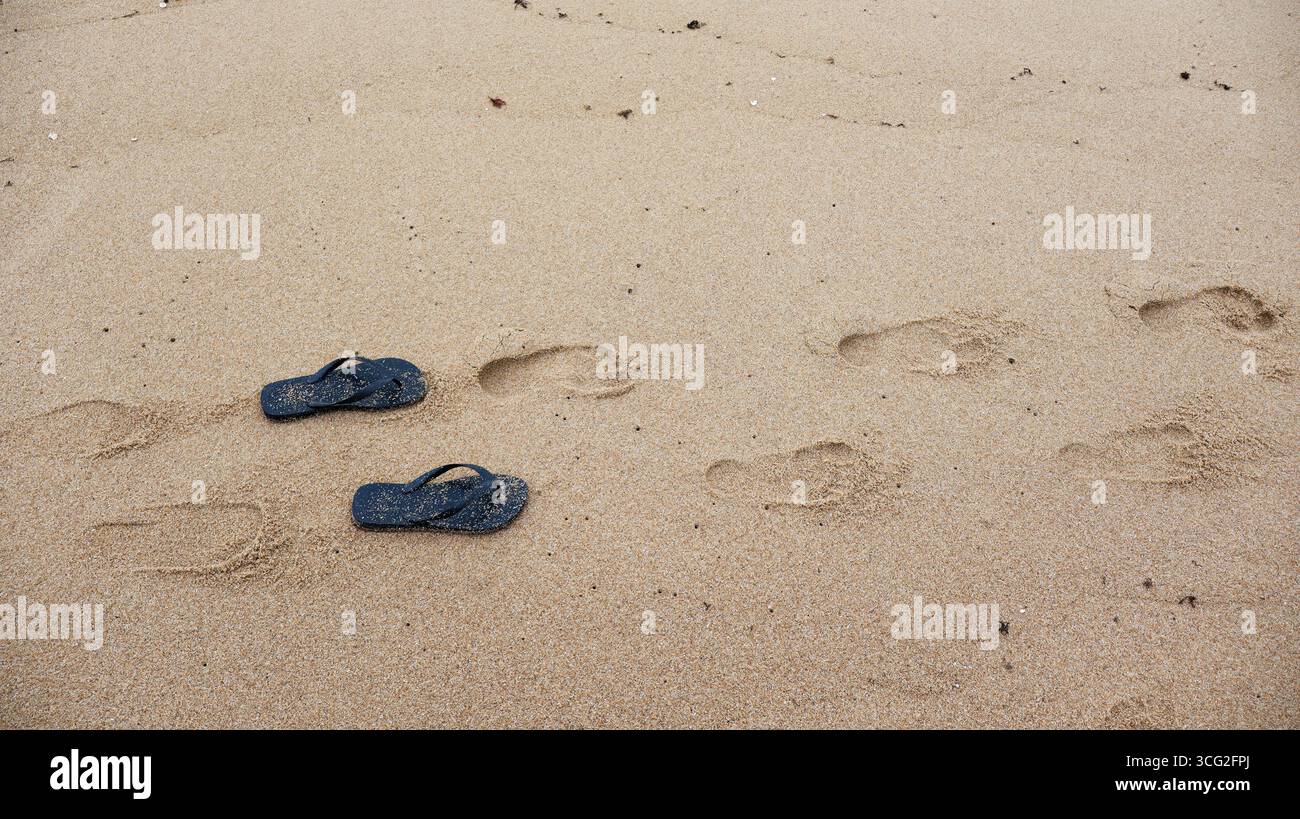 Footprints of a person in the sand on the beach, leaving sandals behind ...