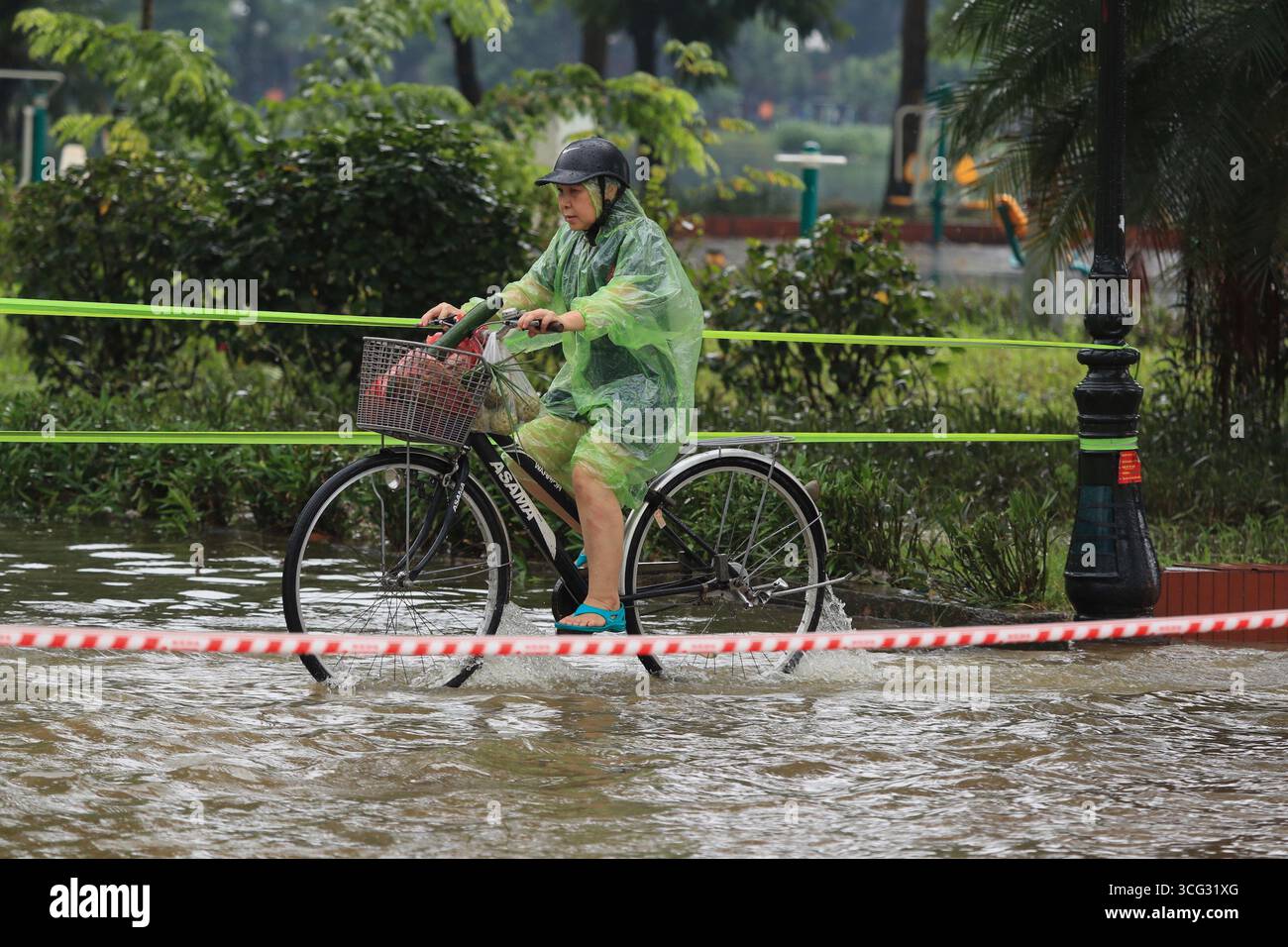 A woman rides a bicycle on a flooded street caused by Typhoon Kajiki in ...
