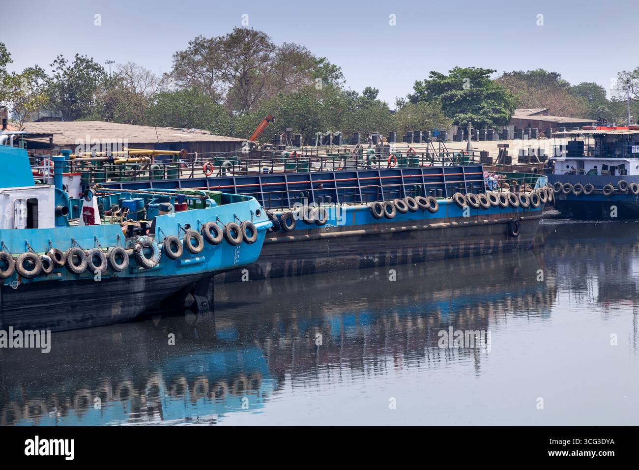 This image shows blue industrial barges docked along a calm waterfront ...