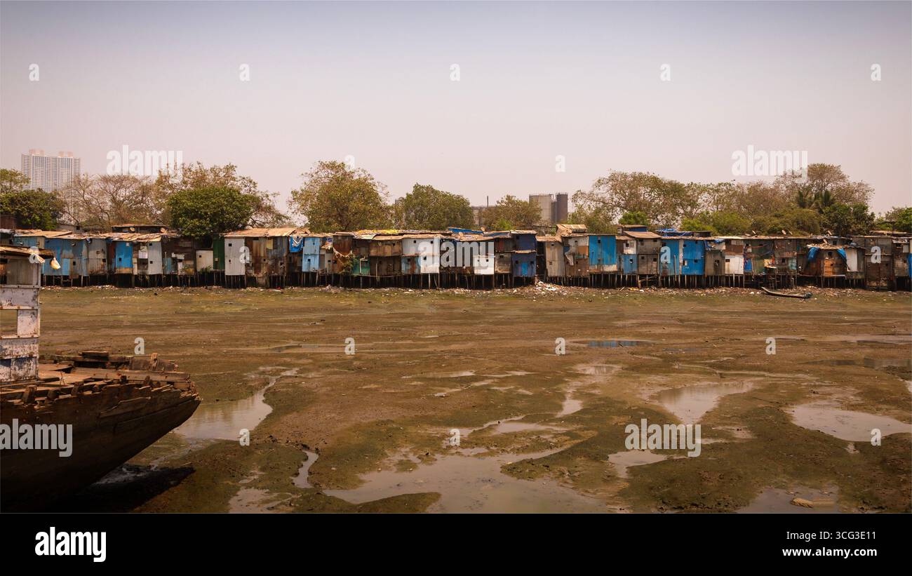 This image depicts a row of makeshift slum houses on stilts, situated ...