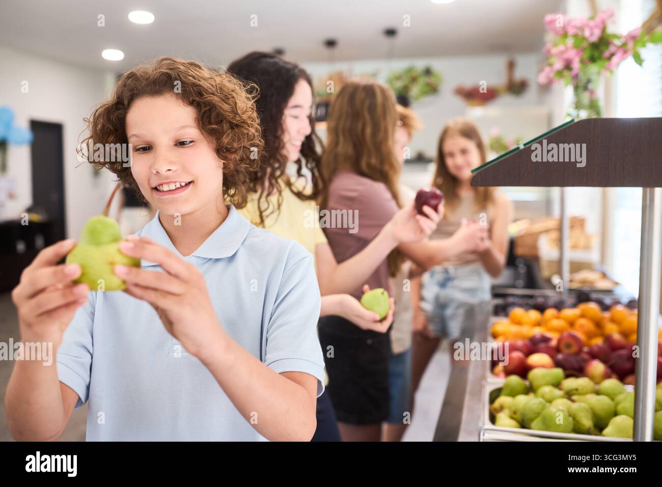 A group of kids gathers at a school cafeteria, selecting fresh fruits ...