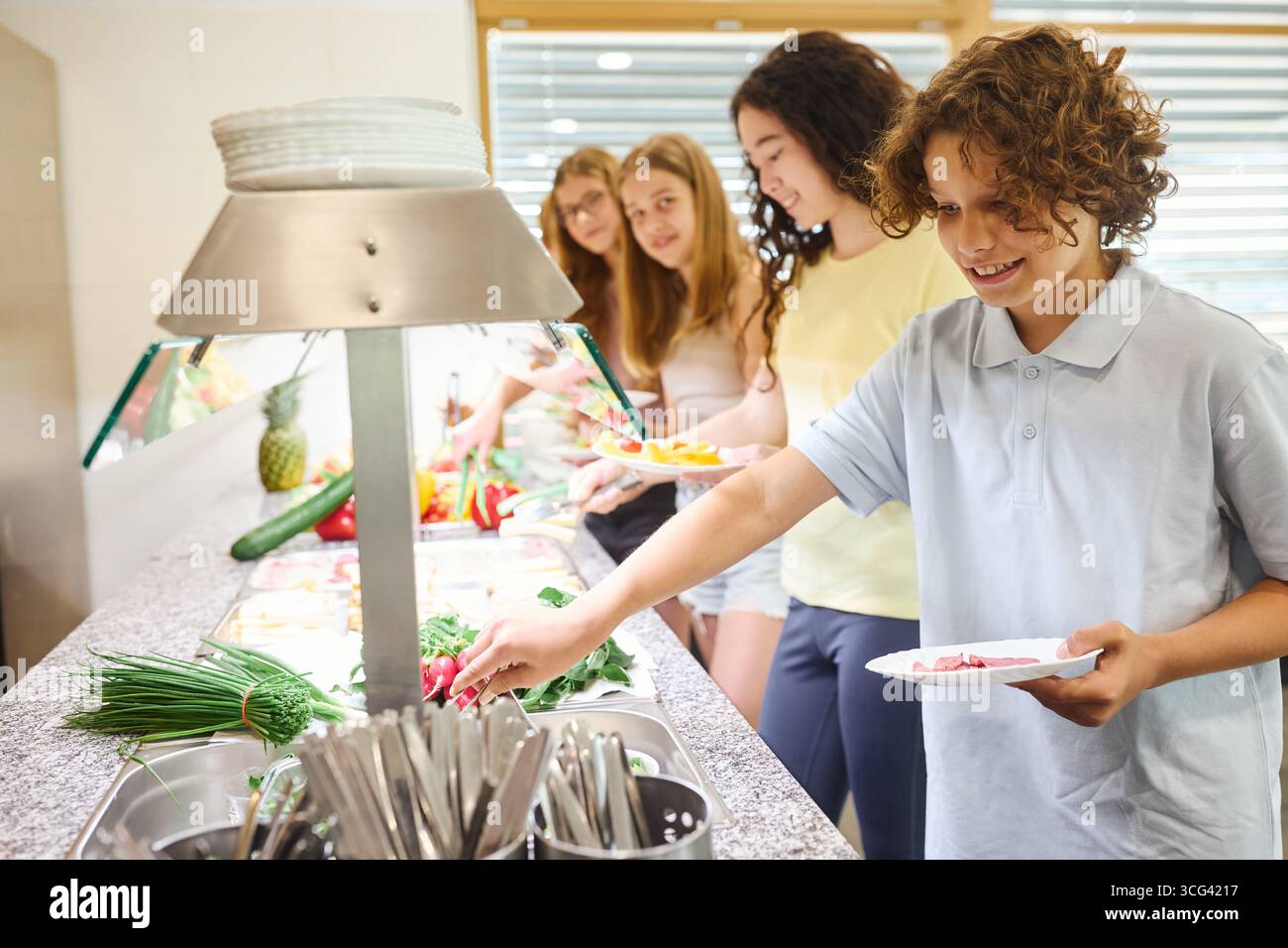 Students standing at a cafeteria buffet, choosing fresh produce and ...