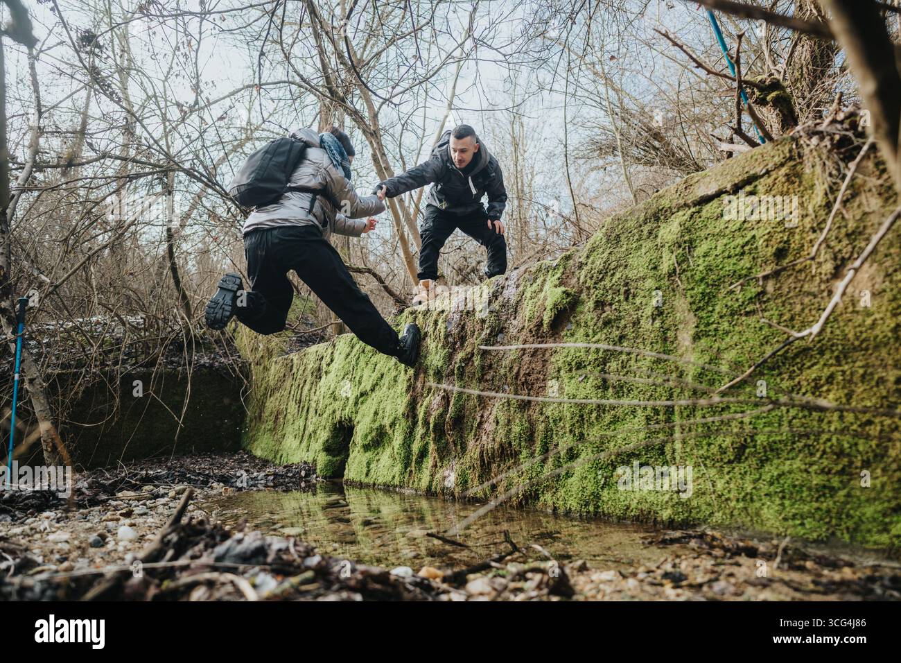 Two hikers helping each other cross a muddy forest stream Stock Photo ...