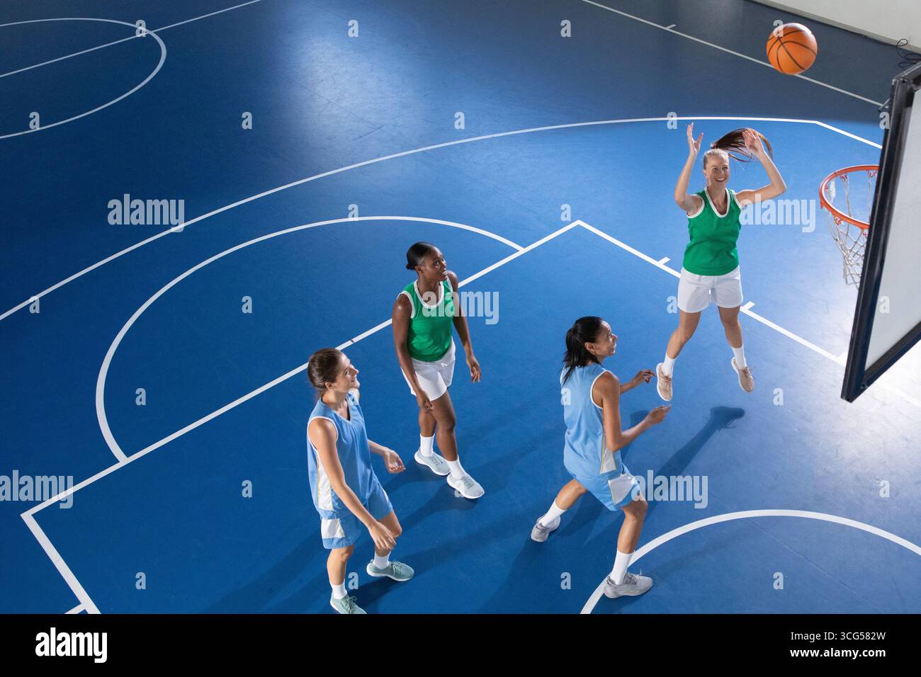 Diverse female players shooting and guarding basketball hoop on court ...