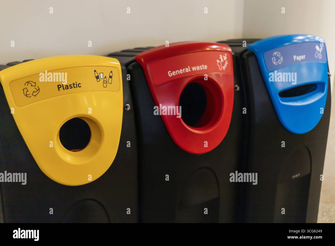 Three waste bins in a public space are clearly labeled for plastic ...