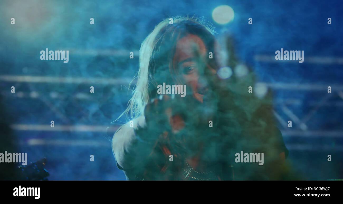 Pointing female singer standing amid haze under blue lights on concert ...