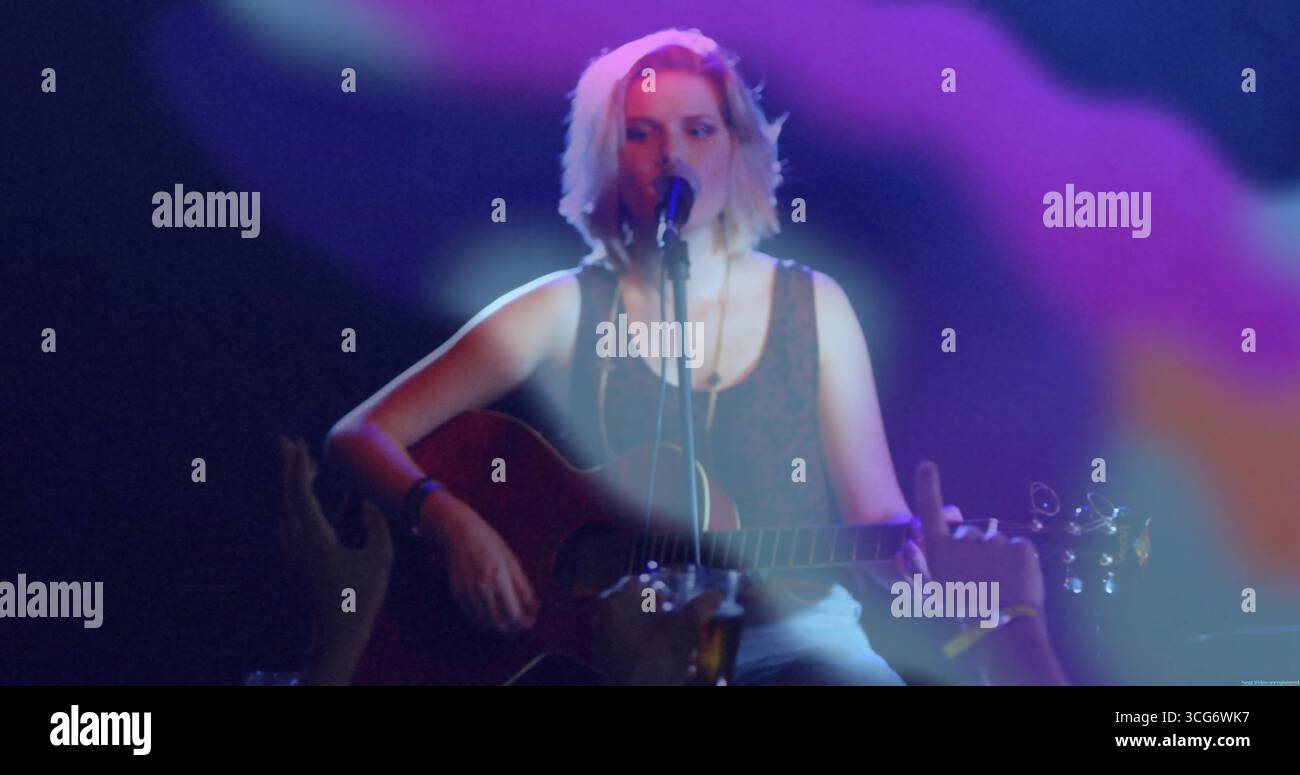 Singing teenage musician strumming acoustic guitar at music venue with ...