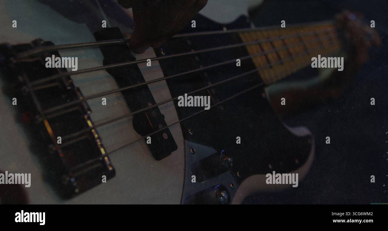 Plucking white electric bass guitar strings in dimly lit studio, over ...
