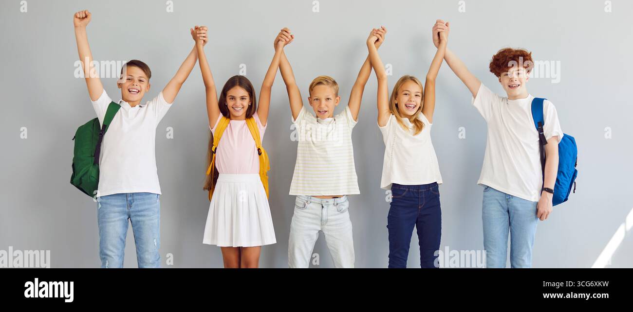 Happy school children standing on gray background holding hands up and ...