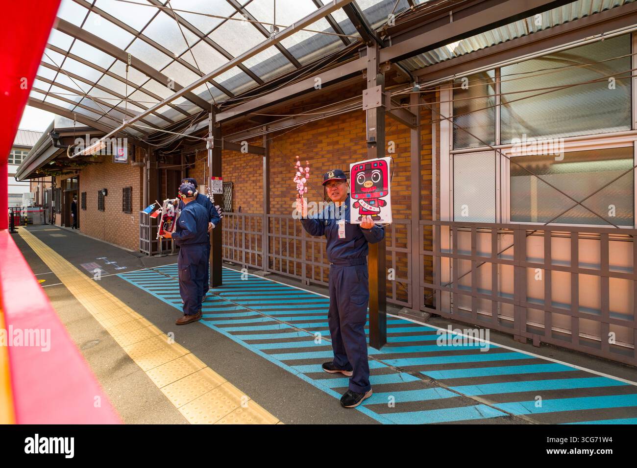 Railway workers standing on train platform waving to departing Sagano ...