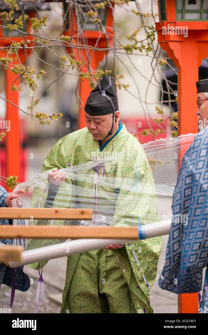 A Shinto priest in traditional green robes and a black headdress using ...