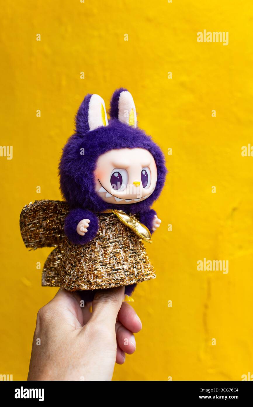 Purple colour Labubu in gold shiny dress posing against yellow ...