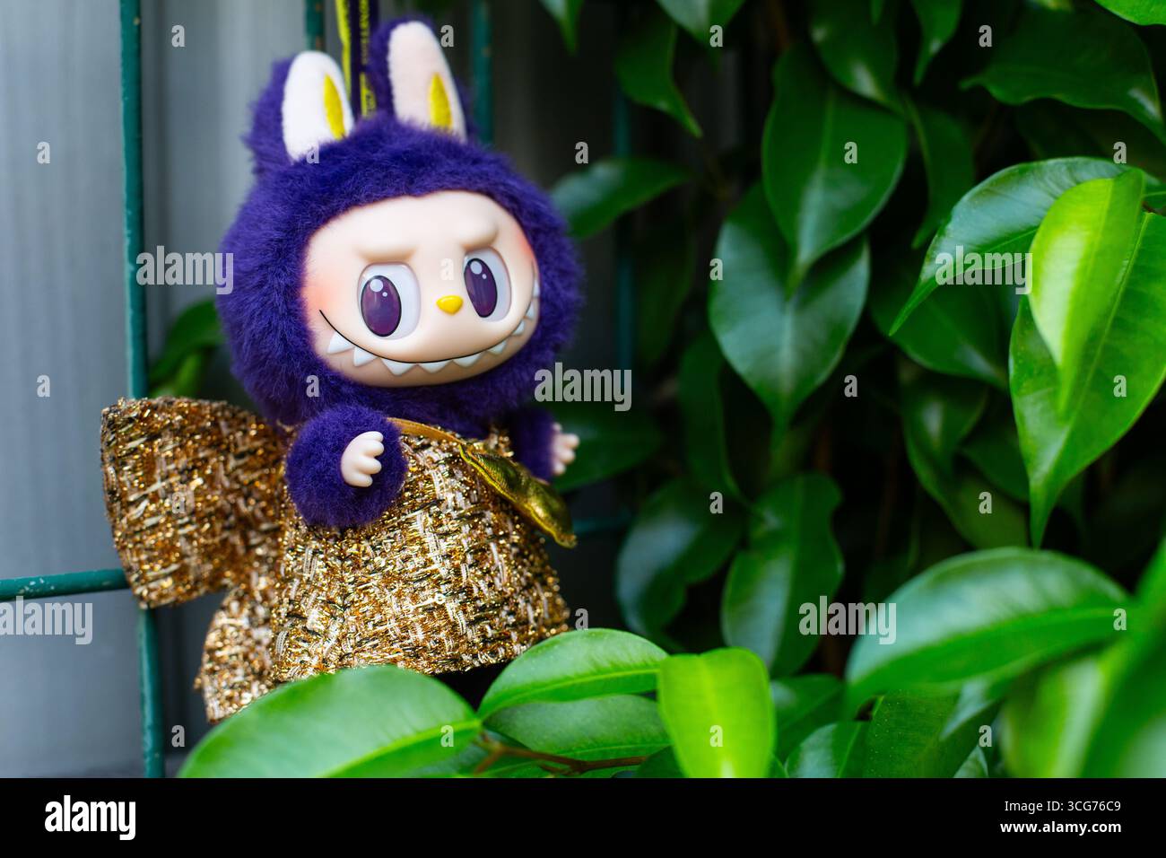 Purple colour Labubu in gold shiny dress posing on green scerny, street ...
