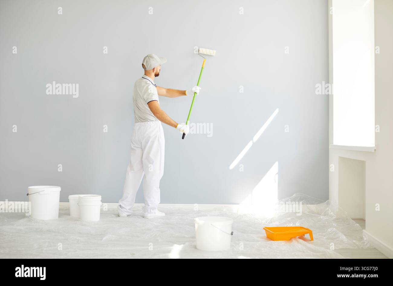 Professional male painter in white uniform painting light grey wall in ...