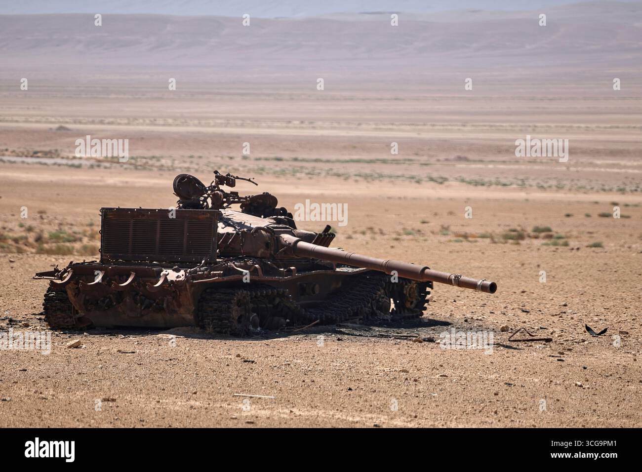 An abandoned, burned-out tank sits in the middle of a desert near the ...