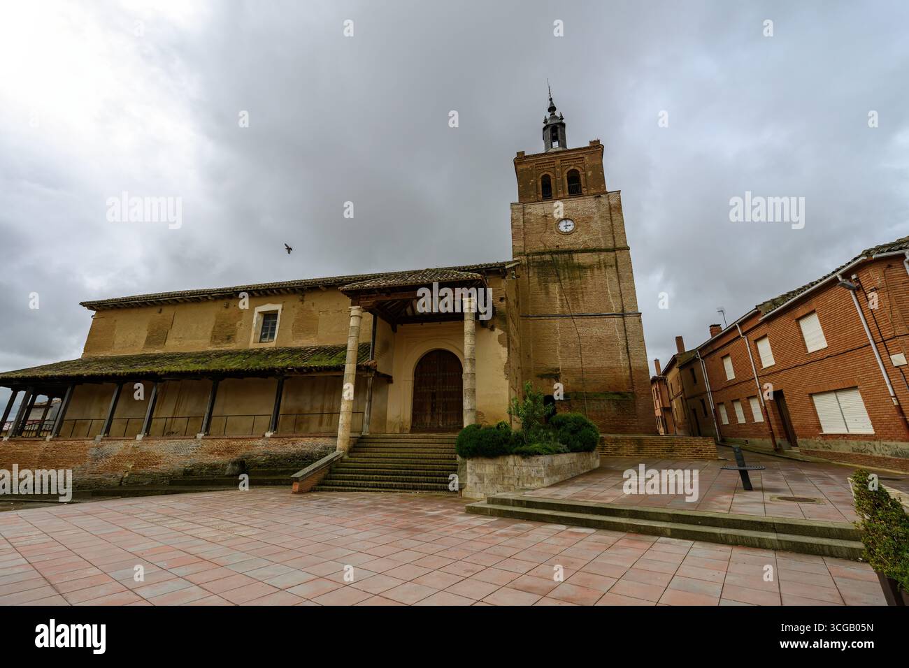 Church with brick clock tower, arched porch and wooden roof, surrounded ...