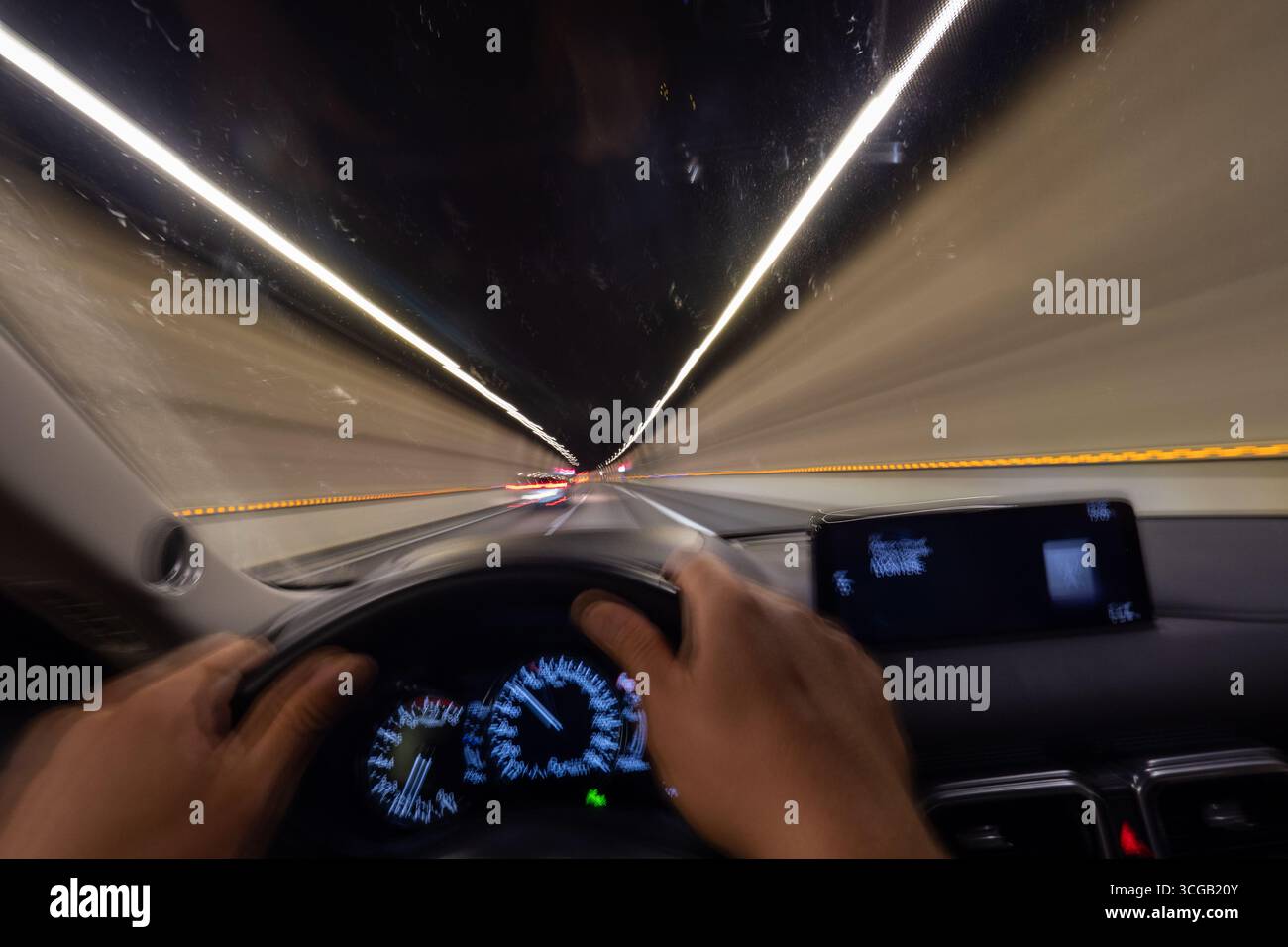 Gripping steering wheel, driver navigating illuminated tunnel, blurred ...