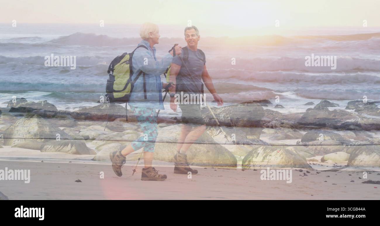 Using trekking poles couple hikers walking along beach at sunrise, with ...