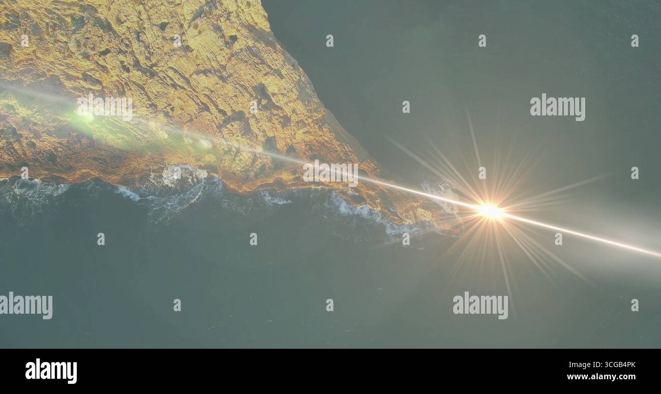 Rocky peninsula extending into calm teal ocean at sunset from above ...