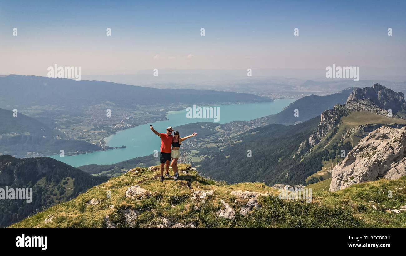 Young couple standing on cliff edge overlooking Lake Annecy and French ...