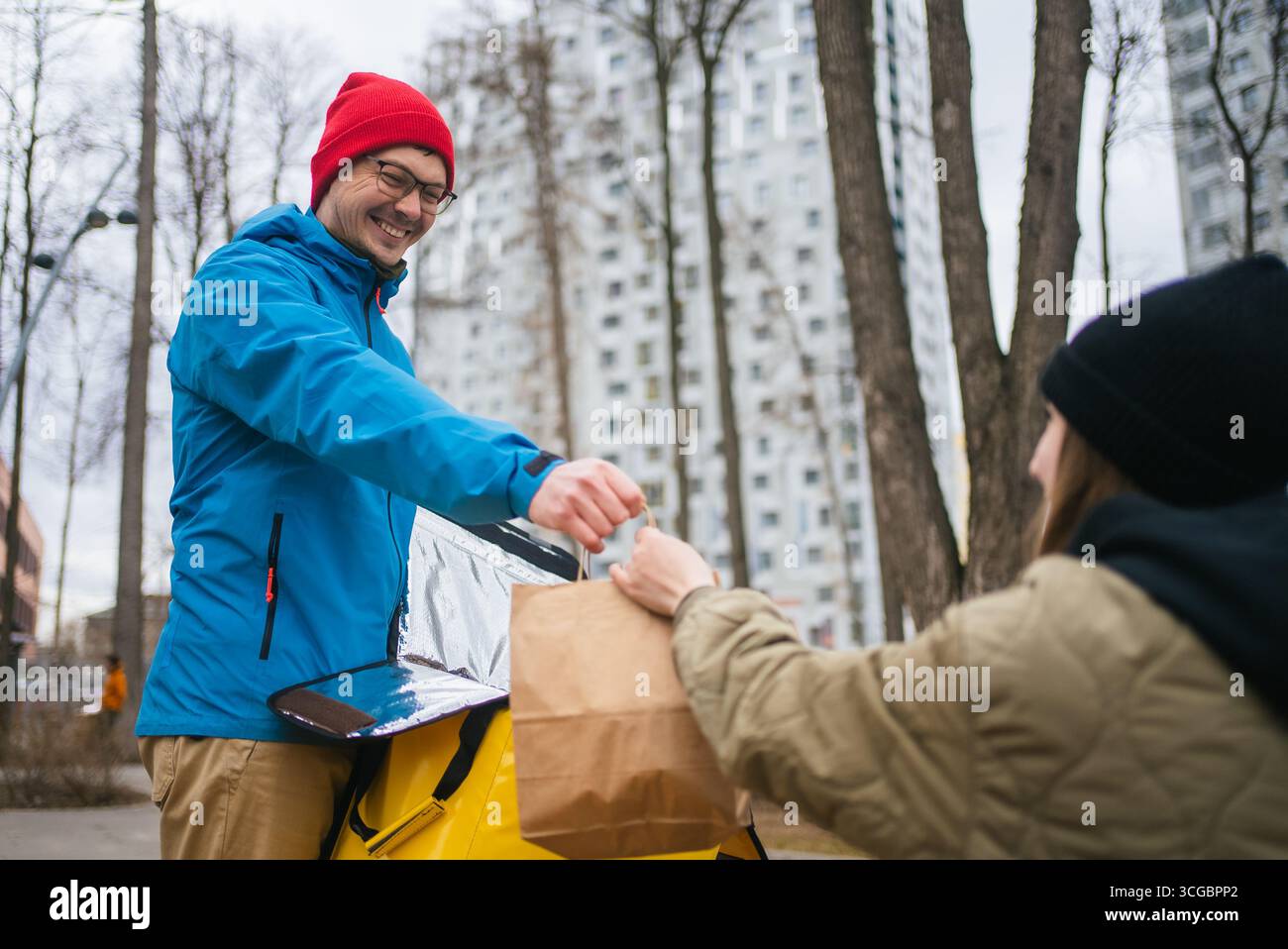 Smiling delivery man handing over a paper bag filled with takeaway food ...